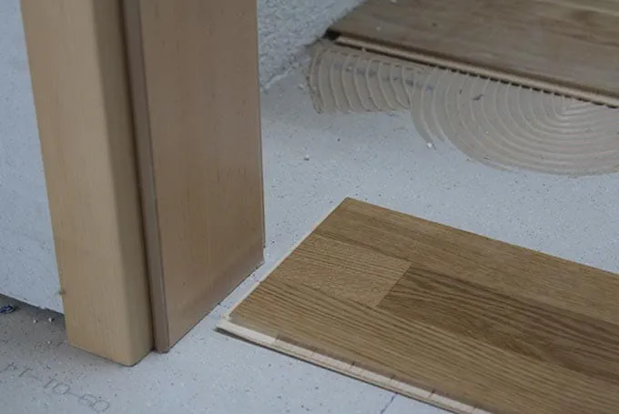 Shorten a door frame and lay laminate under the door frame
